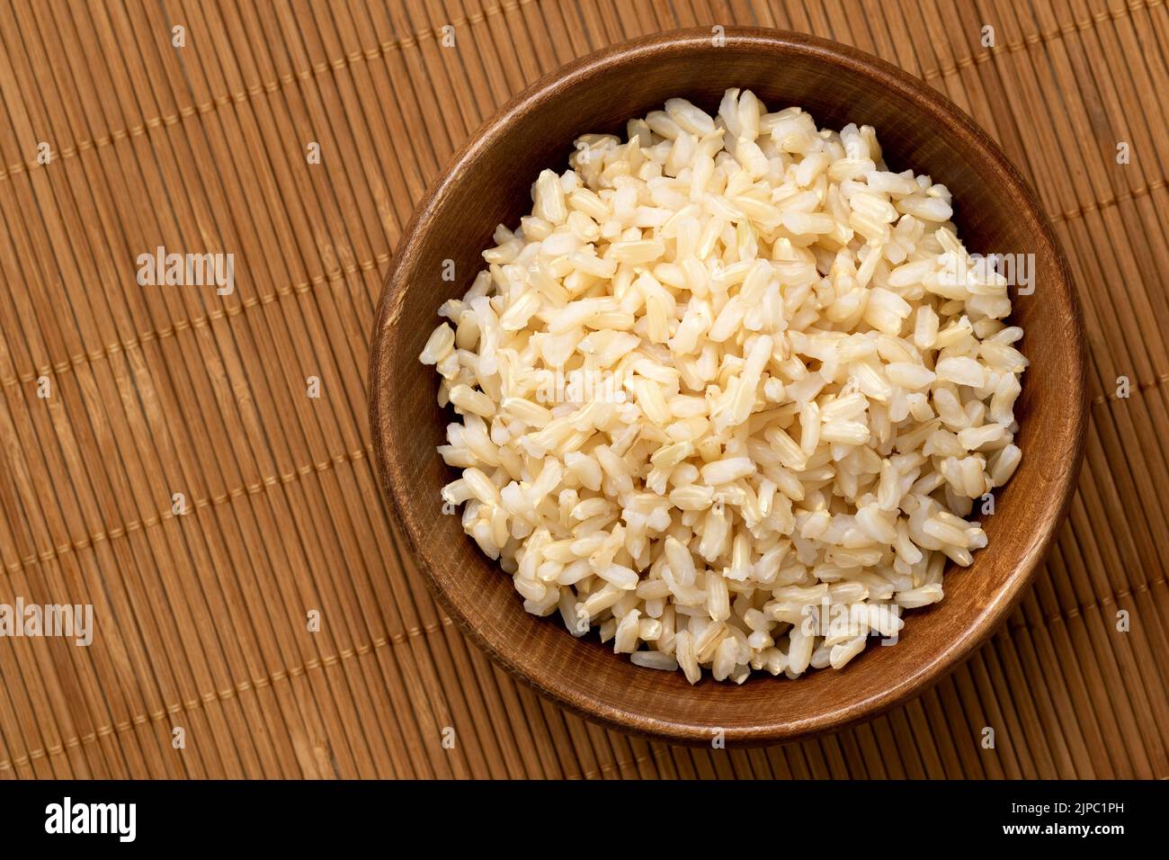 Brown cooked rice in a brown wood bowl isolated on bamboo matt.Top view ...