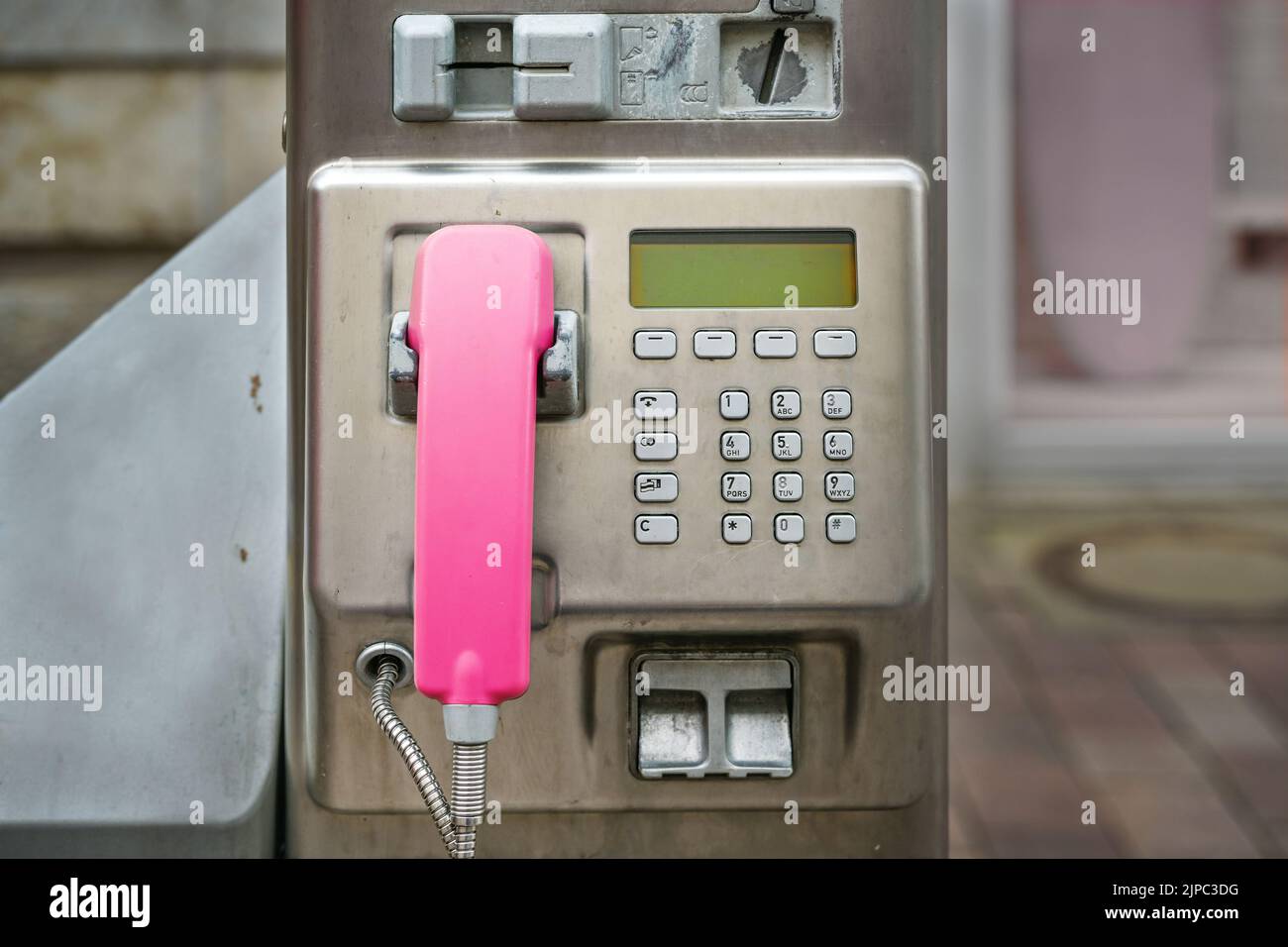 Public pay phone made of scratched metal with a pink handset, insert ...