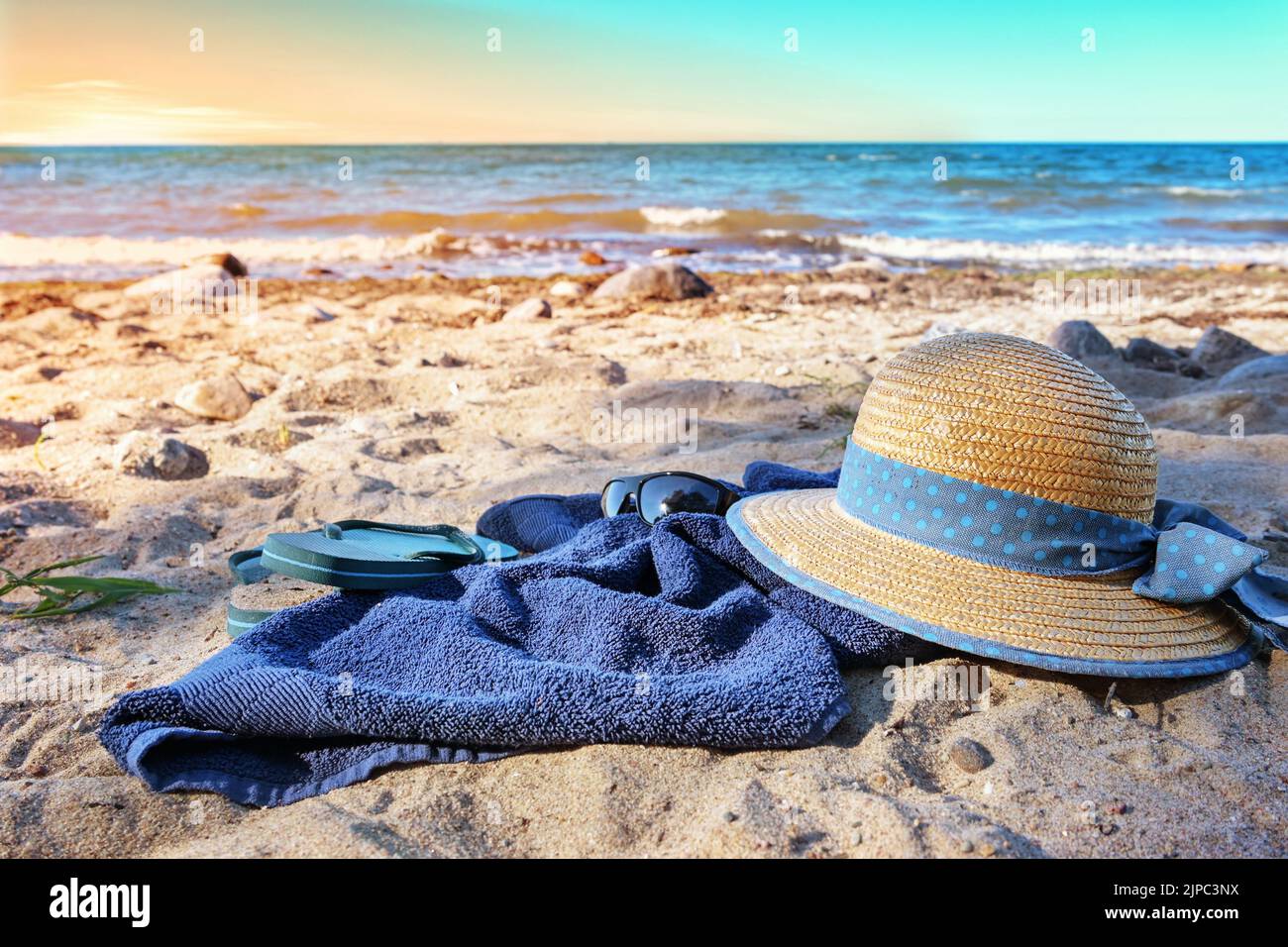Summer vacations on the beach, straw hat and a blue towel, sand and water, tourist resort on the ...