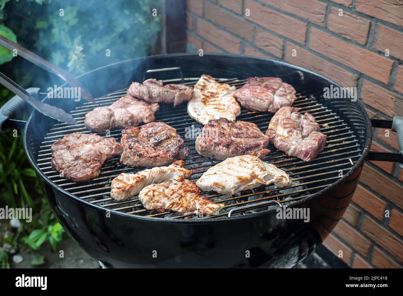 Steaks of various meats on a mobile round grill are roasted over ...