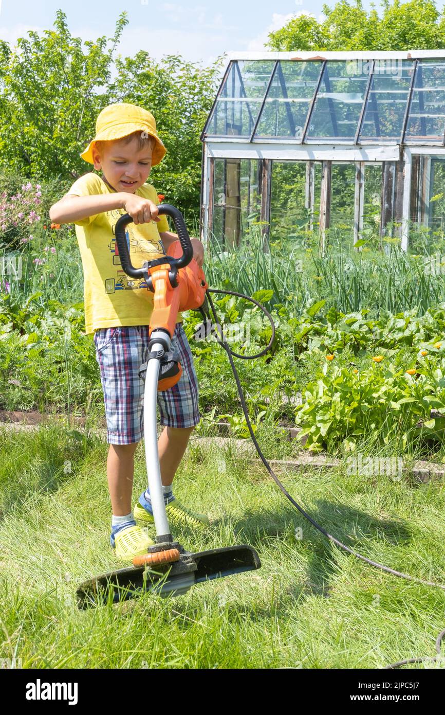 Portrait a boy with an electric lawn mower mowing the lawn. Beauty boy ...