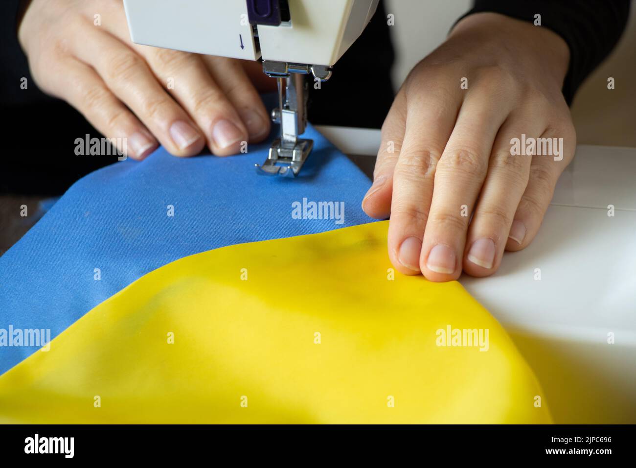 A girl sews the flag of Ukraine at home on a sewing machine, the ...