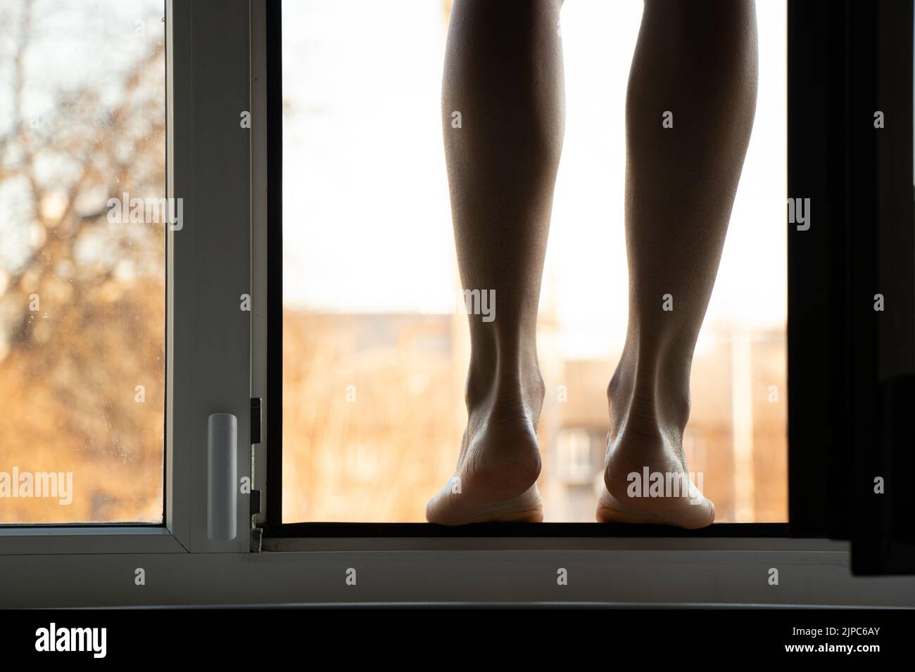 A young girl is standing on the window in her apartment, committing ...