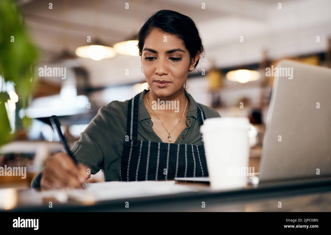 Small business owner working on a budget in her coffee shop and writing ...