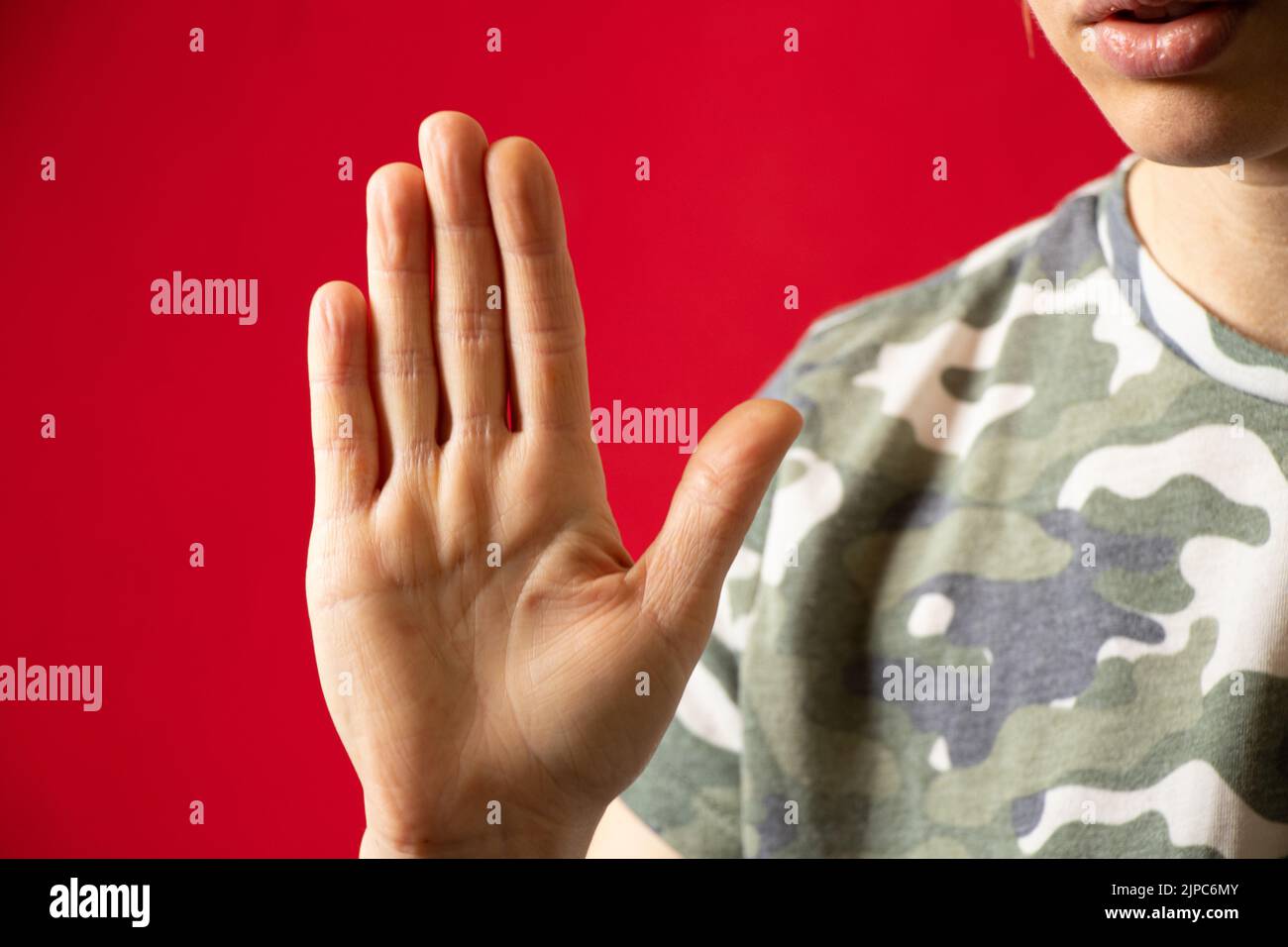 Hand of a girl in a camouflage uniform on an isolated red background ...