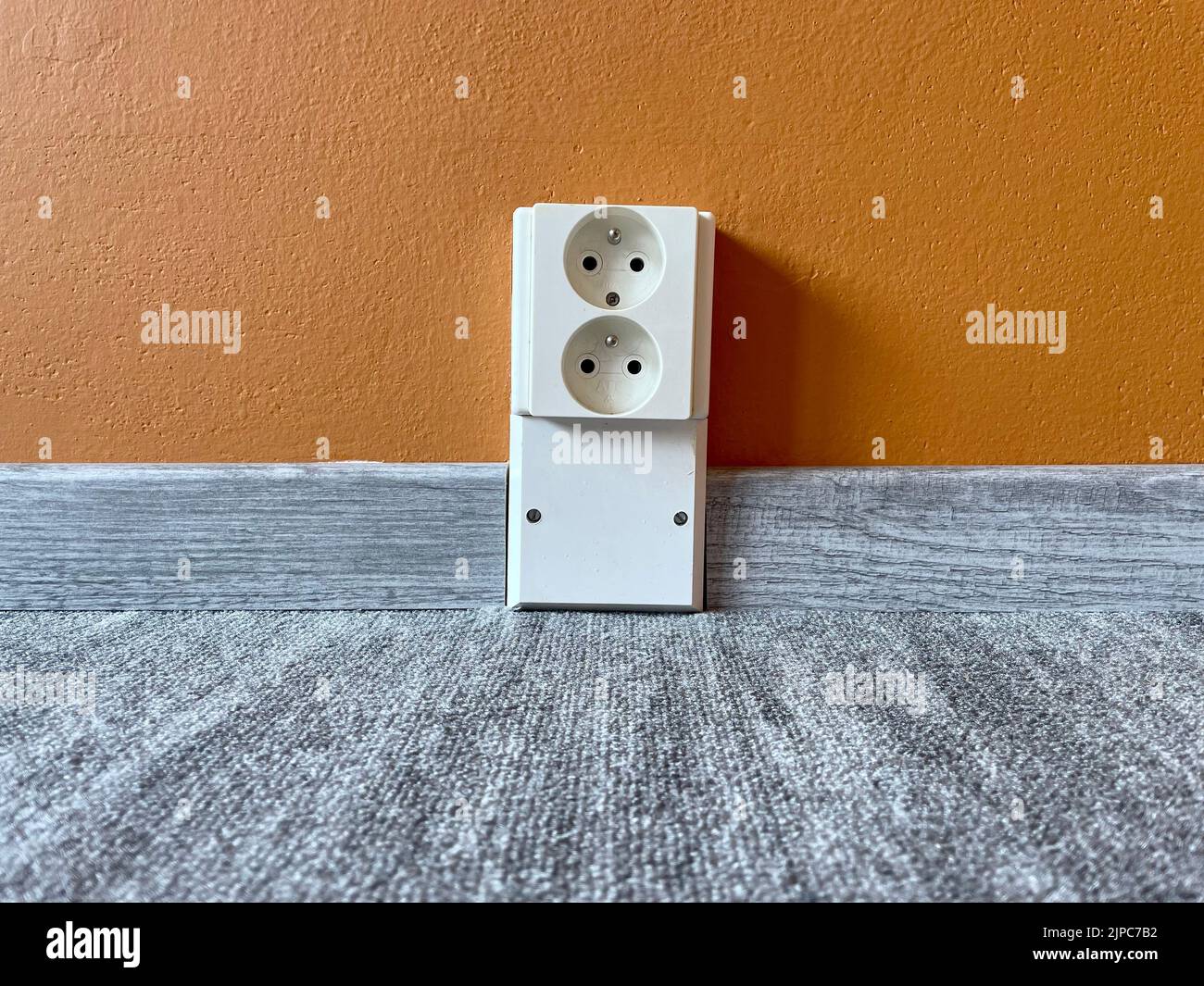 Electric socket by the floor between plastic baseboard with a wooden ...