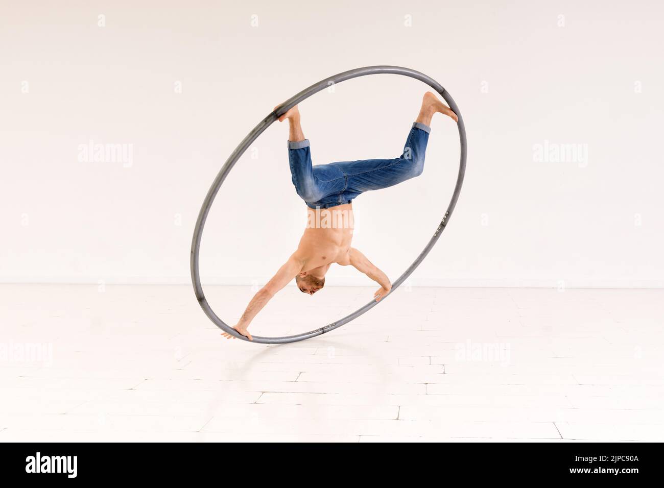 Full body of strong shirtless male acrobat performing coin trick with ...