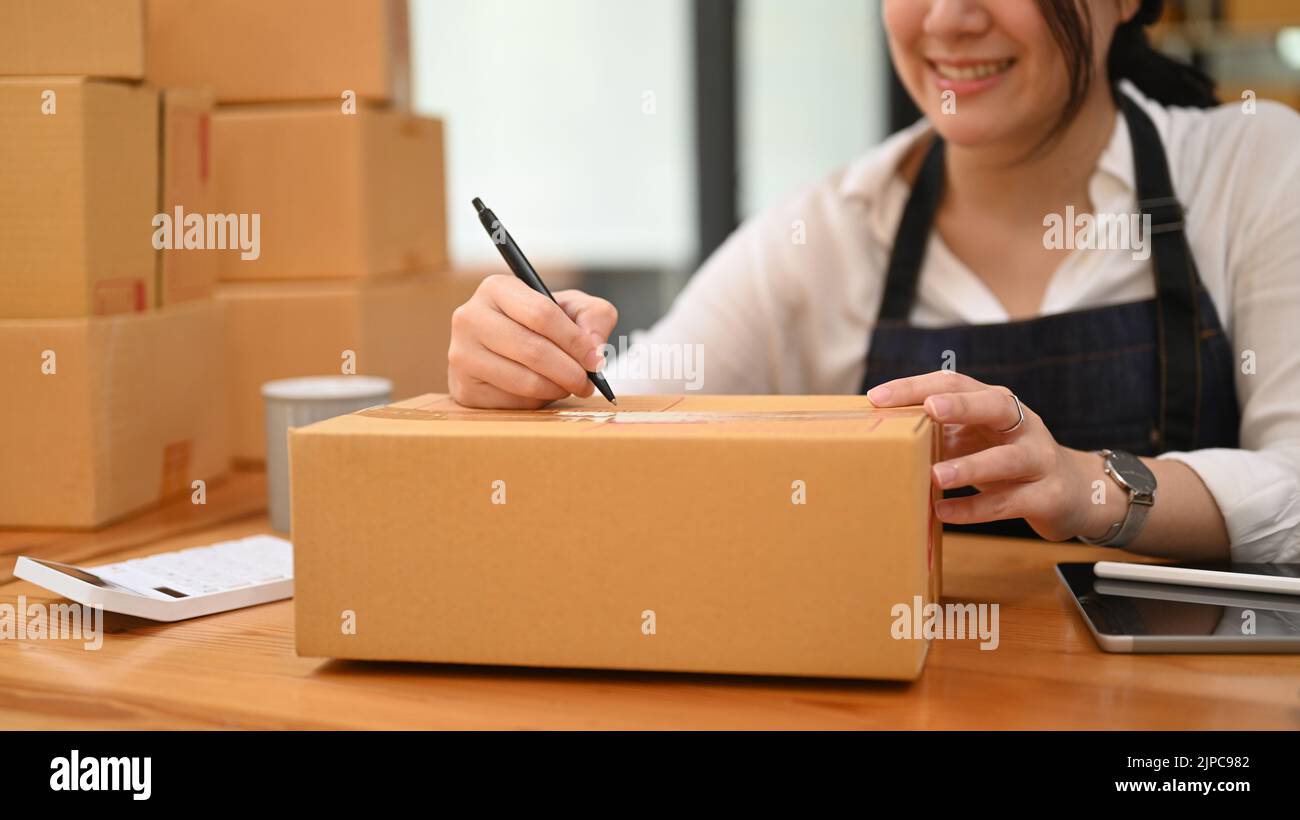 Female small business entrepreneur writing address on cardboard box ...