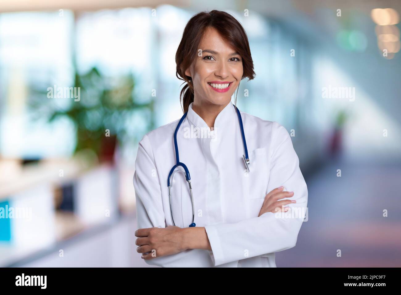 Portrait of female doctor with arms crossed while standing at clinic’s foyer. Confident ...