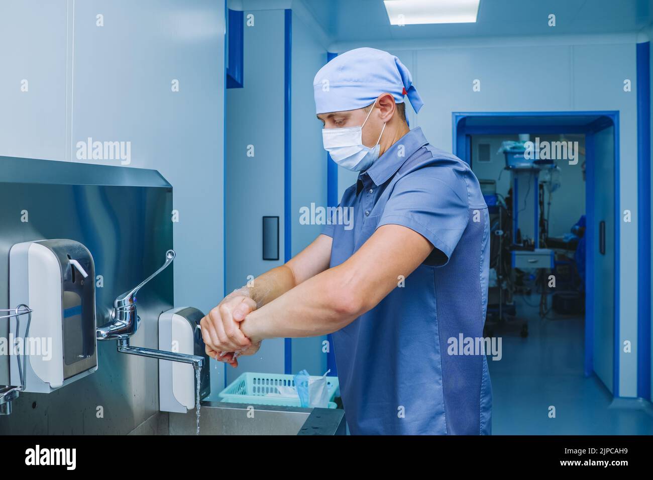 A male surgeon in a hospital sanitary room washes his hands before ...