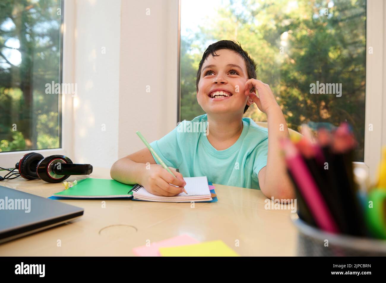 Smart boy, student of online primary school, thoughtfully writting an ...