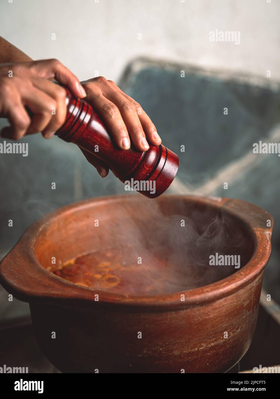 A vertical shot of person adding pepper into a clay pot Stock Photo - Alamy