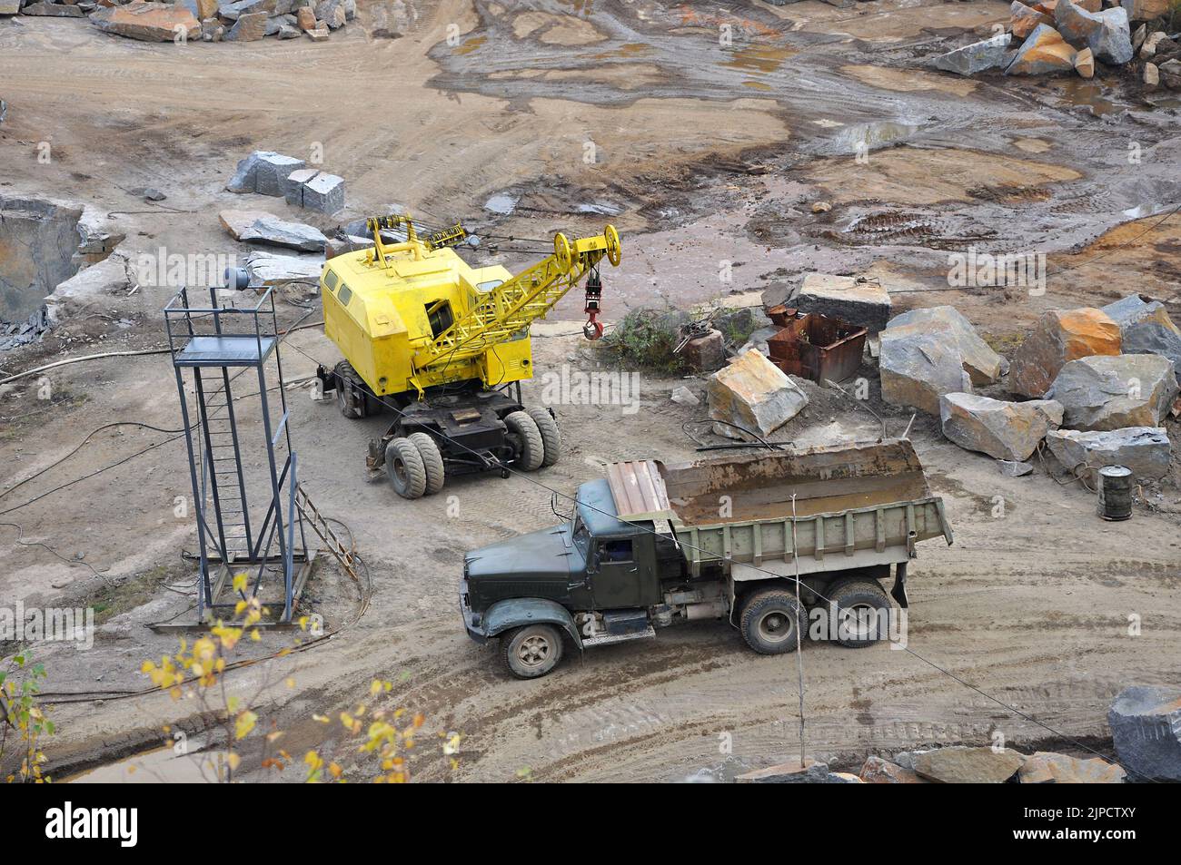 Work site in granite quarry with old rusty empty truck, yellow crane ...
