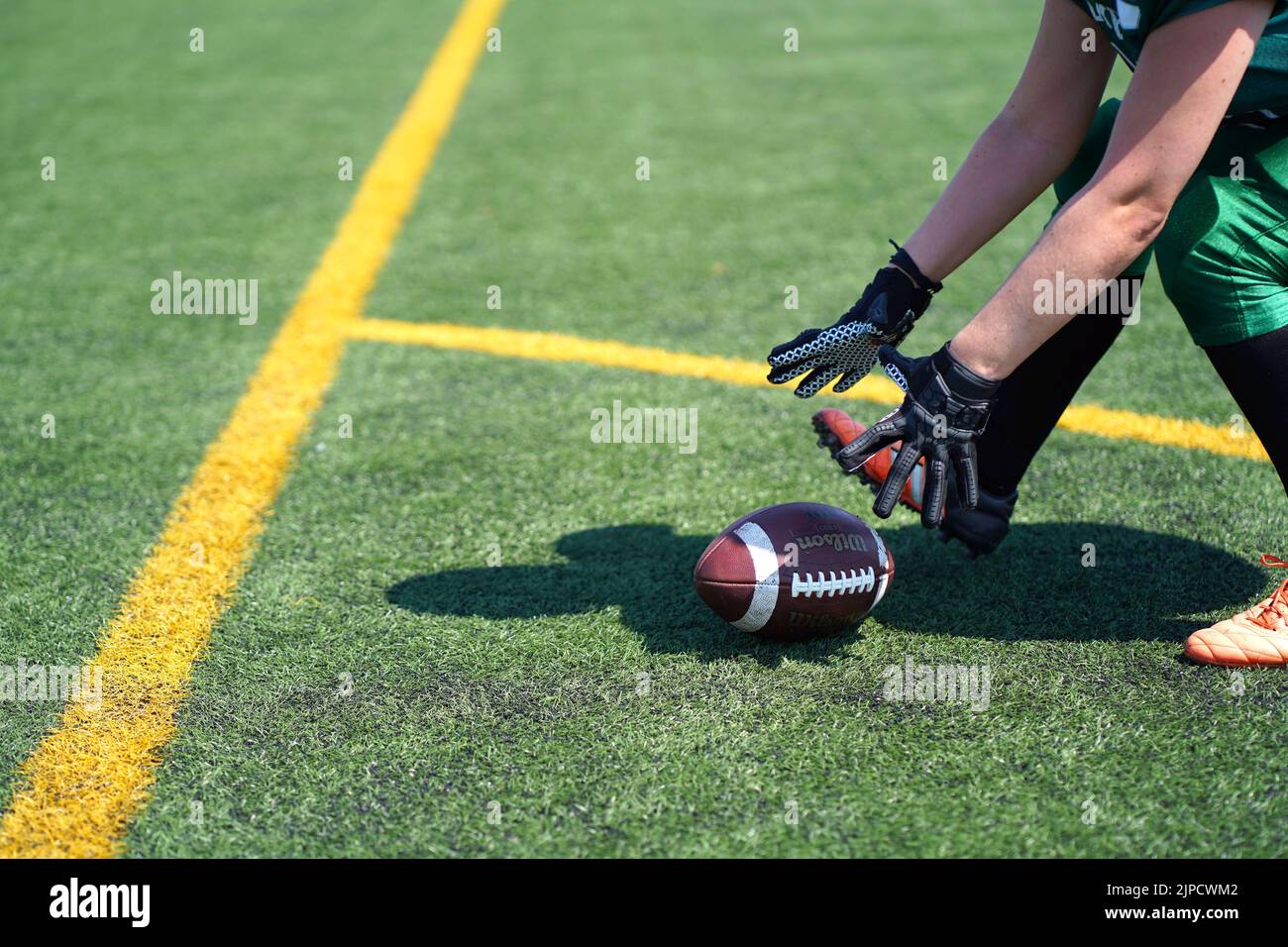 White female gloved hands reach for a Wilson American Football rolling ...