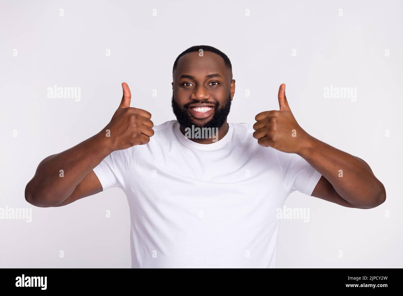 Photo of confident cute man wear casual t-shirt smiling showing thumbs ...