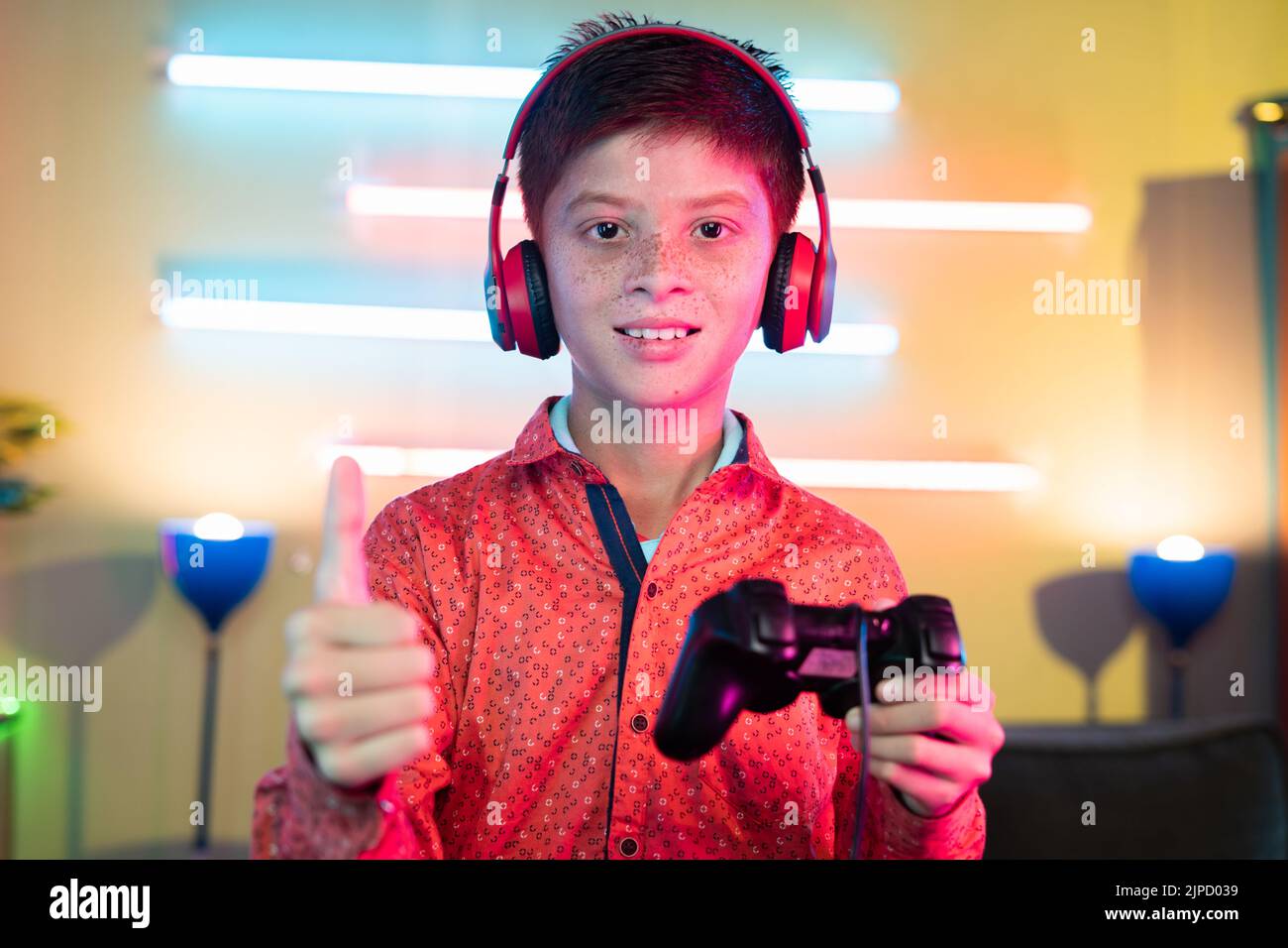 young Teenager kid with headphones holding gamepad by showing thumbs up ...
