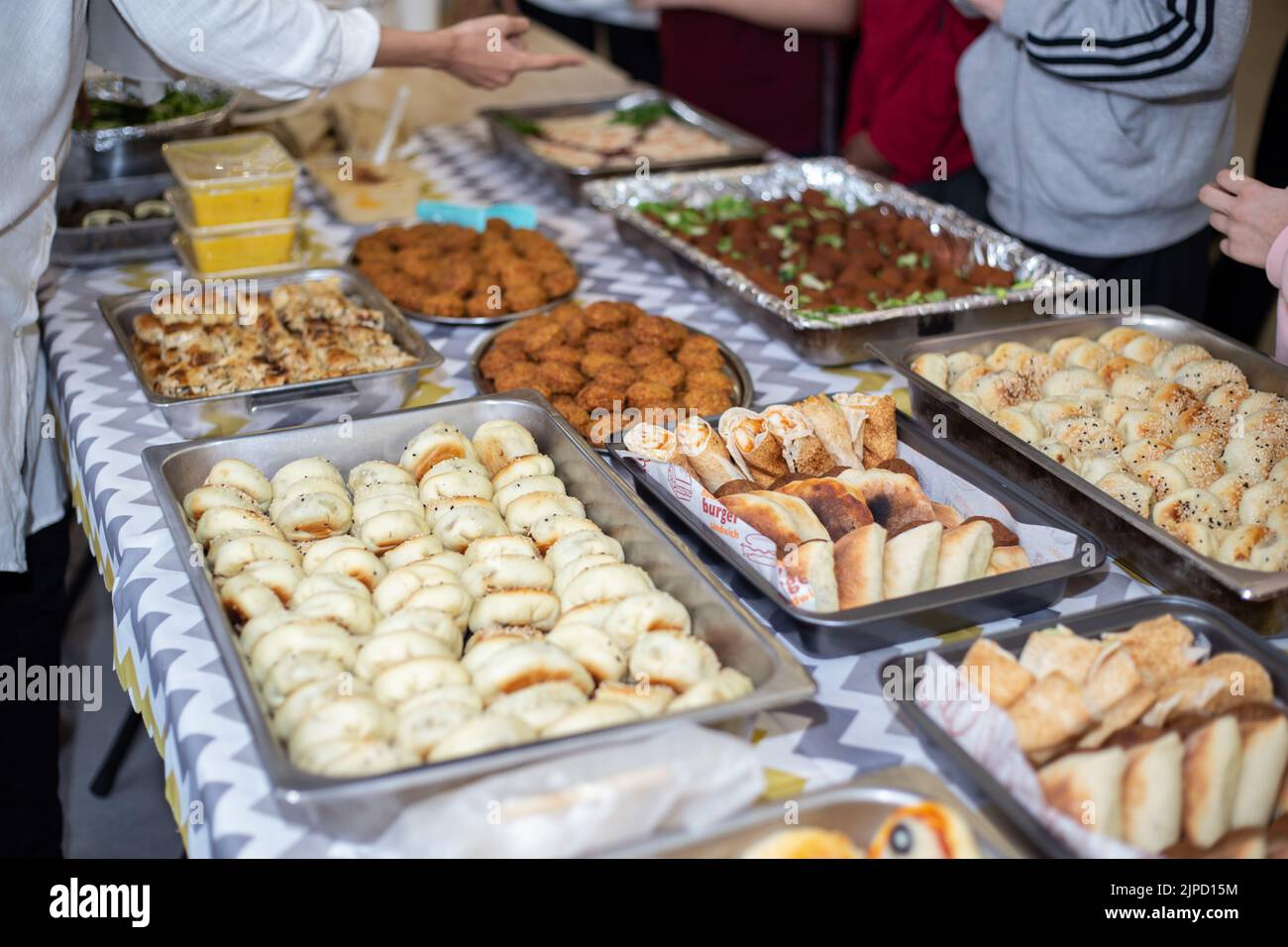 A table of delicious sweets and bakeries with people standing around ...