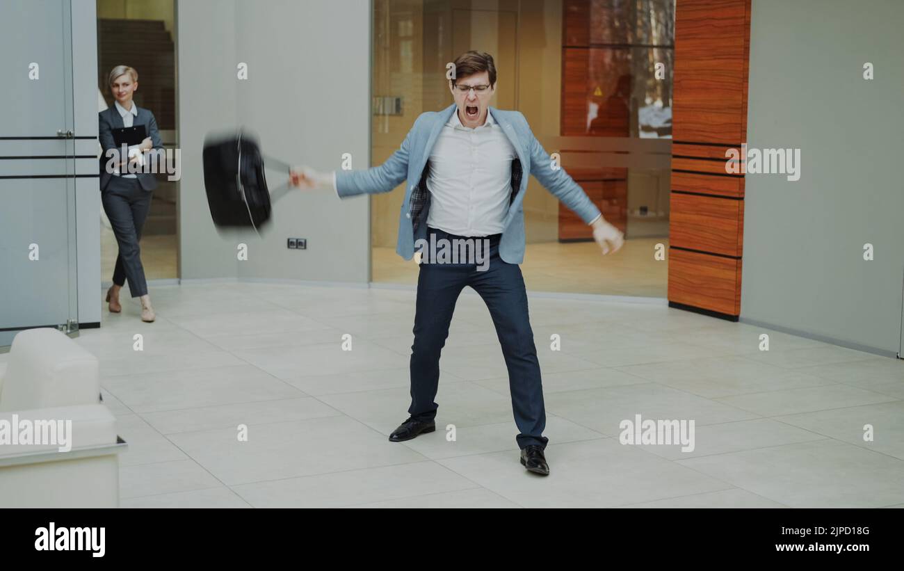 Crazy businessman dancing with briefcase in modern lobby indoors while ...