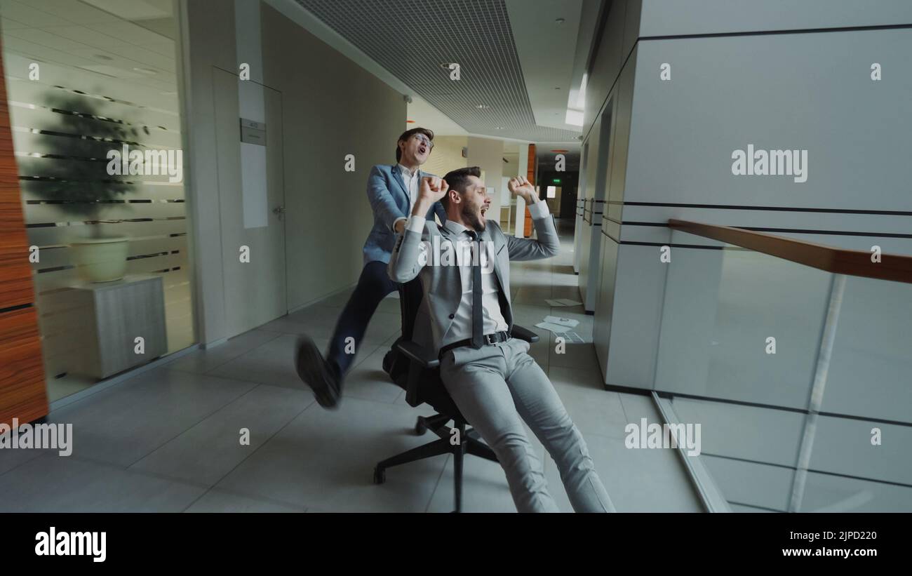 Two crazy businessmen riding office chair and throwing papers up while ...