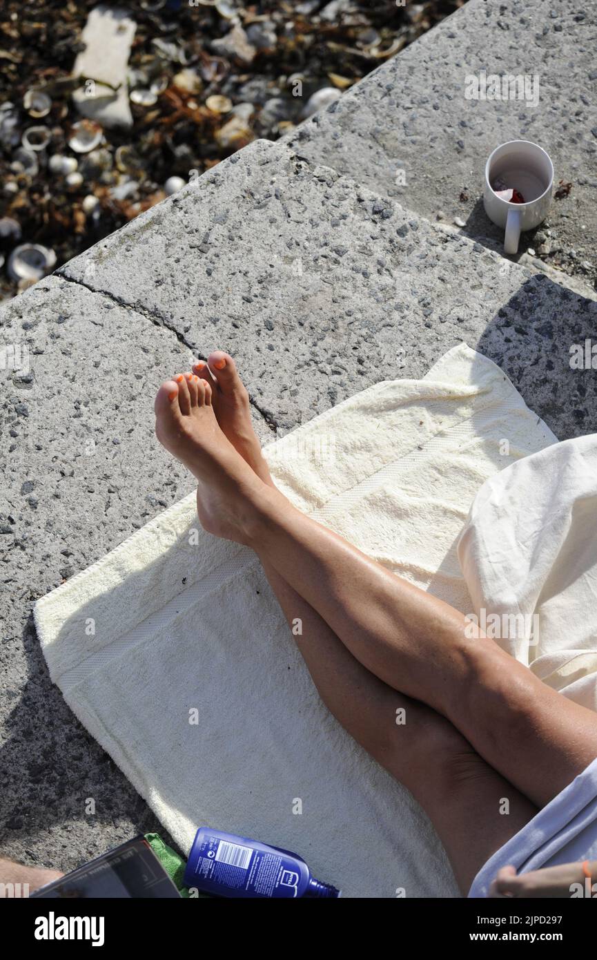Feet Woman with crossed legs relaxing on harbour front in sunshine on towel Stock Photo - Alamy