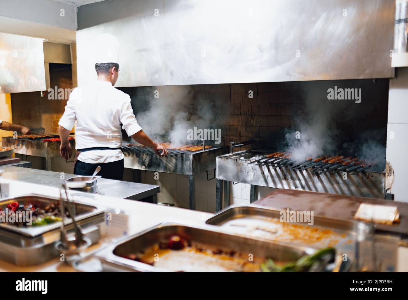Cook in uniform preparing a food on barbecue grill in a kitchen ...
