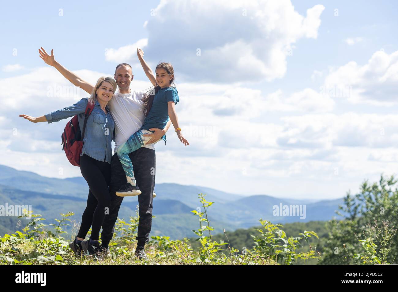 Mother, father hugging son, and daughter in summer mountains. Happy family smiling and standing ...