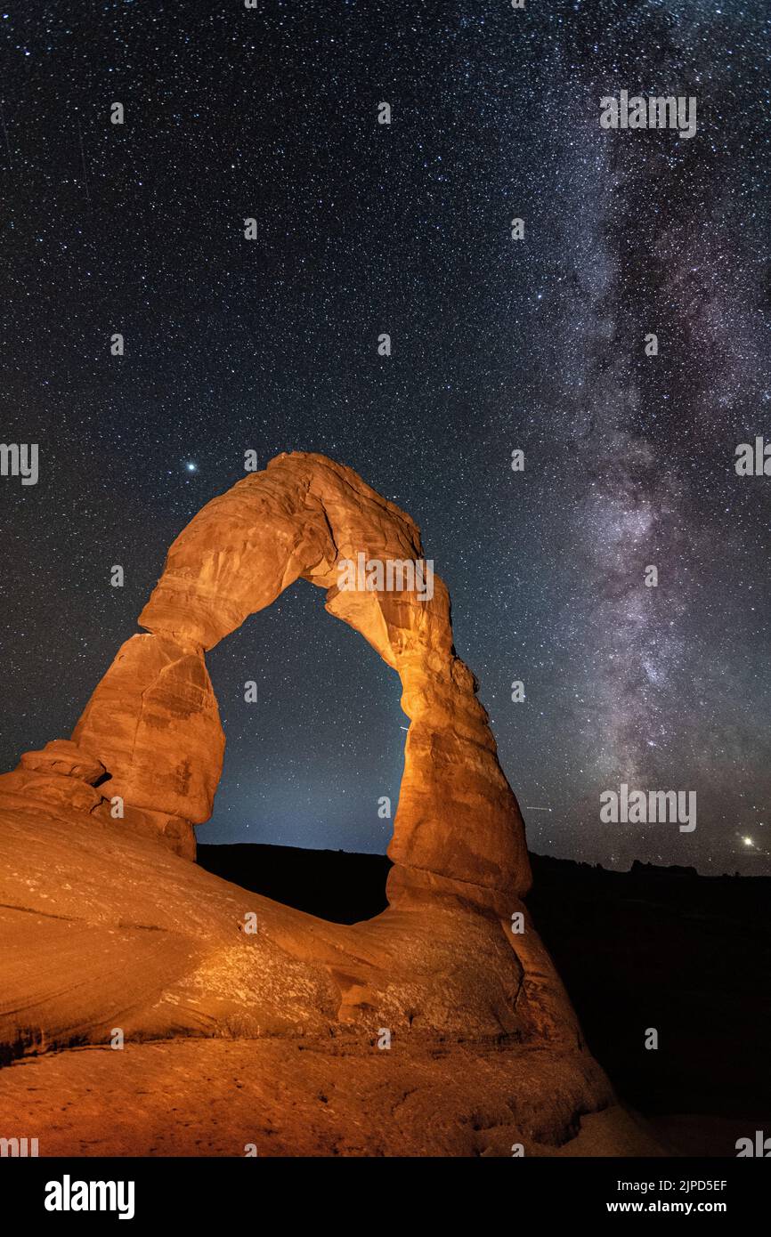 A vertical shot of a stone arch formation under a milky way galaxy sky ...