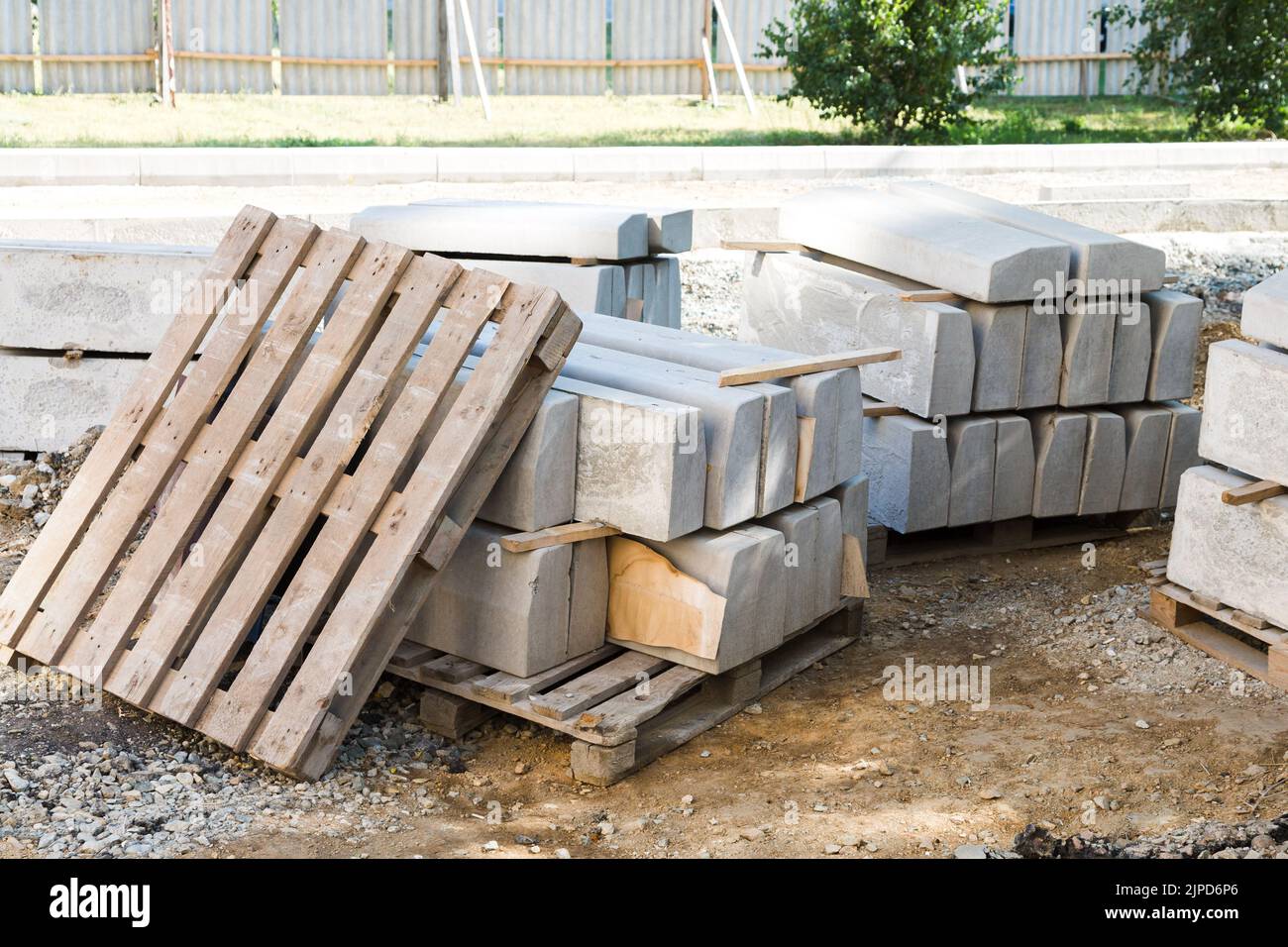 Reinforced concrete blocks neatly stacked on the territory of a fenced construction site, a curb ...