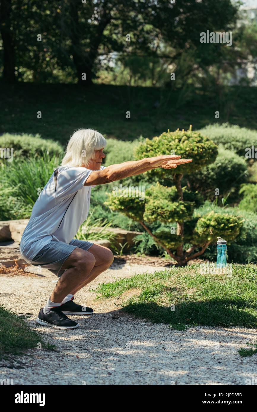 full length of cheerful senior man with grey hair working out with ...