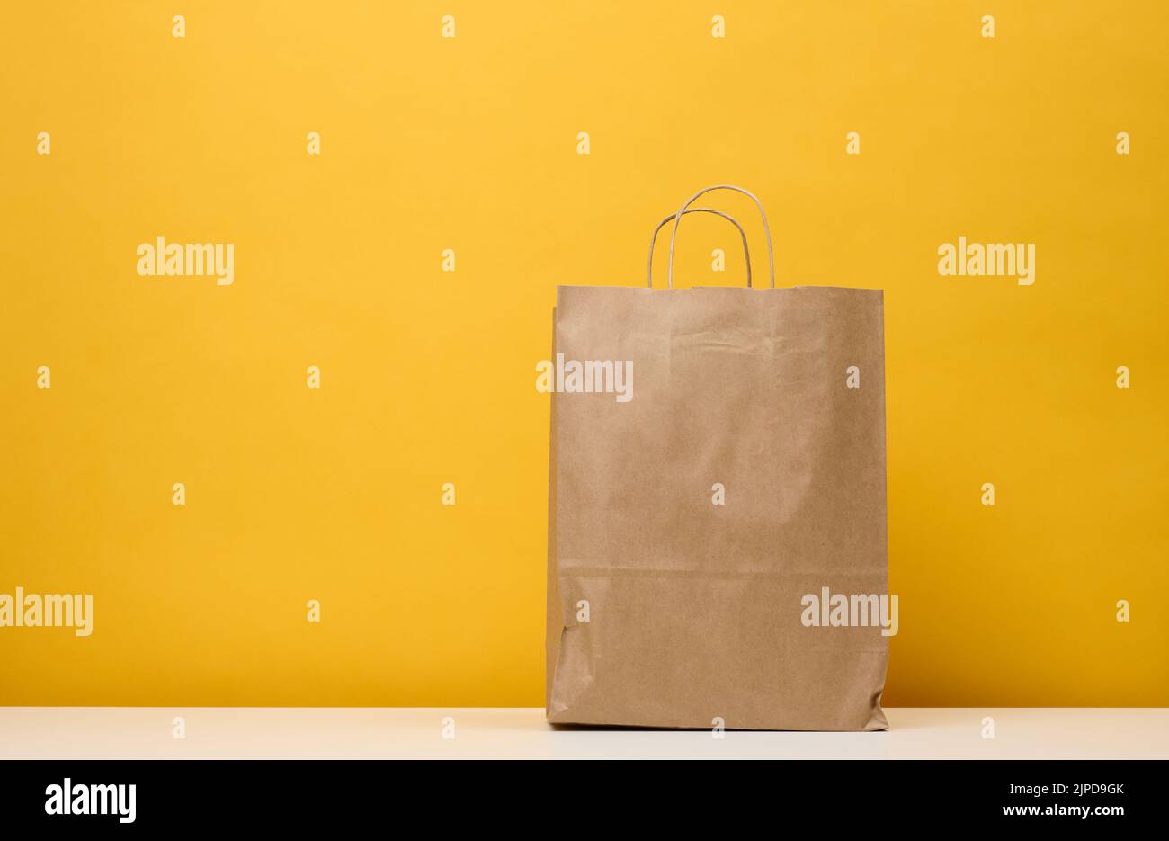 A brown paper bag stands on a white table, yellow background. Product ...