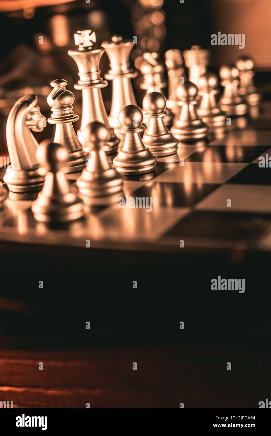 A vertical shot of chess pieces on a board against a blurred background ...