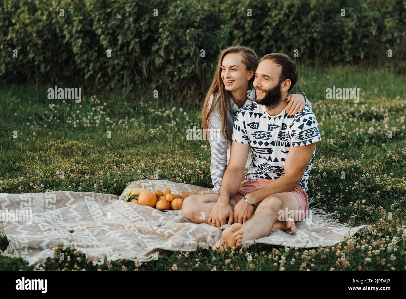 Cheerful man and caucasian woman sitting on blanket and enjoying ...