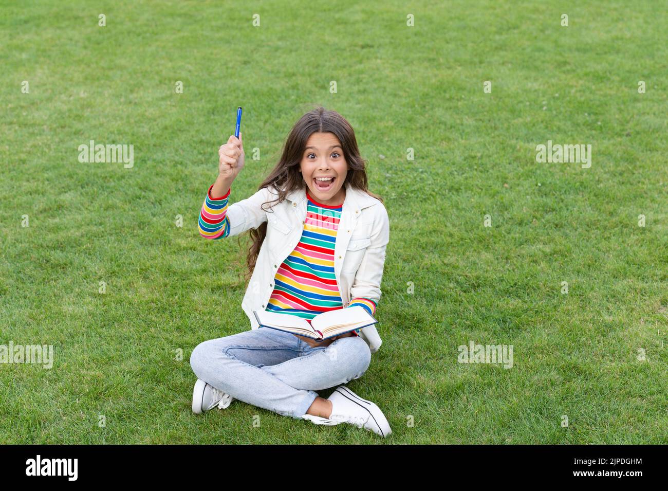 inspired teen girl making notes in notebook sitting on grass. taking ...