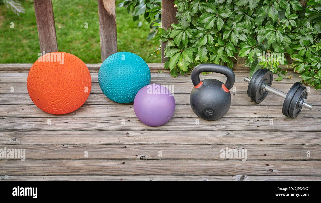 three heavy slam balls, iron kettlebell and dumbbell on a backyard deck ...