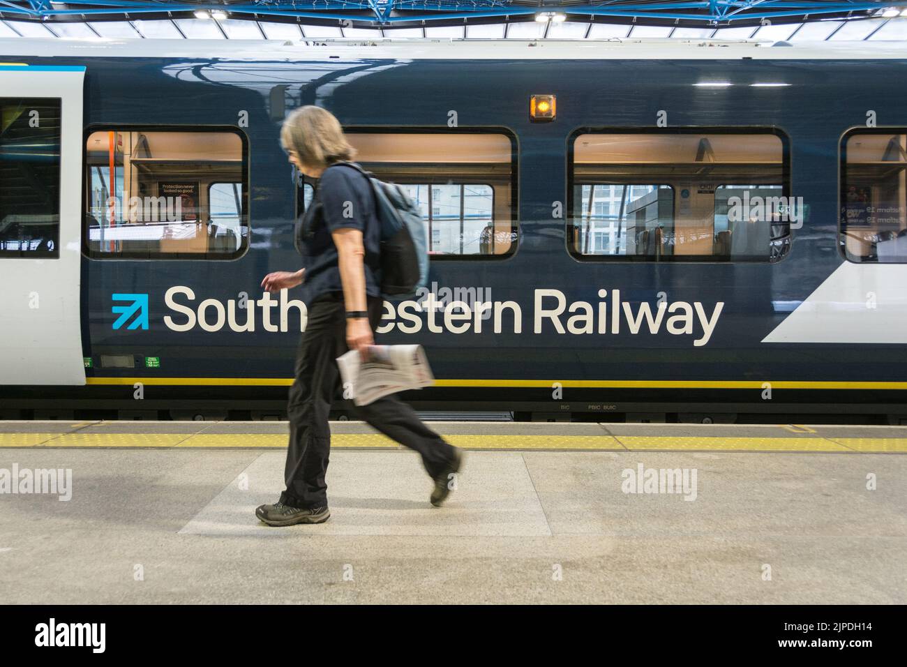 Closeup of a female commuter walking past a South Western Railway (SWR) carriage at London ...