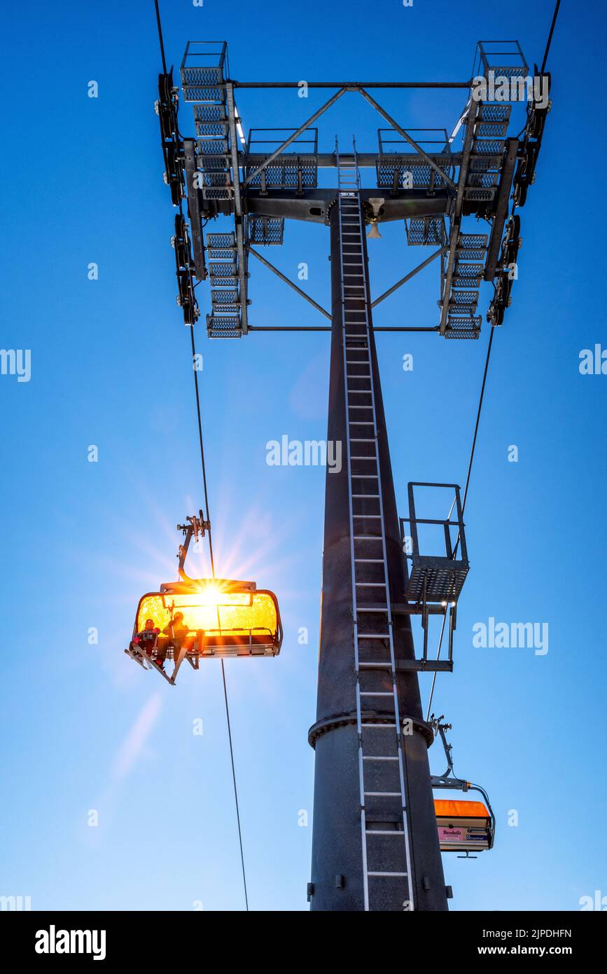 Skiers sitting at ski-lift chair and cable car mast on blue sky ...