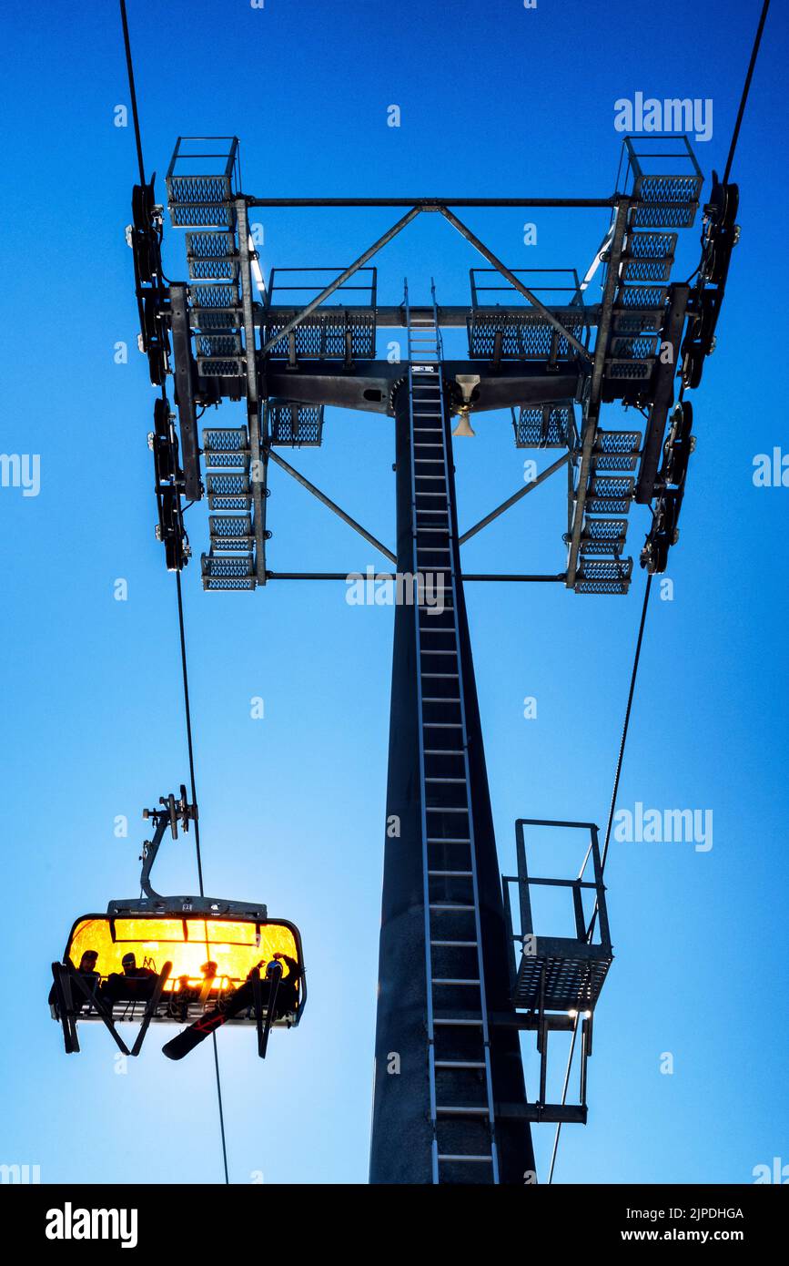 Skiers sitting at ski-lift chair and cable car mast Stock Photo - Alamy