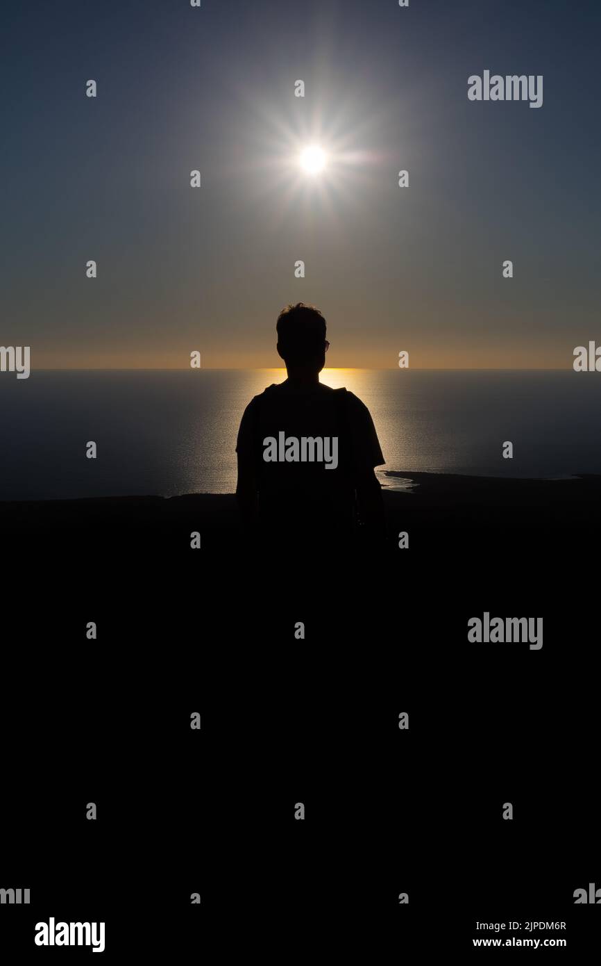 An unidentifiable silhouette of a person under the sun with the sea in ...