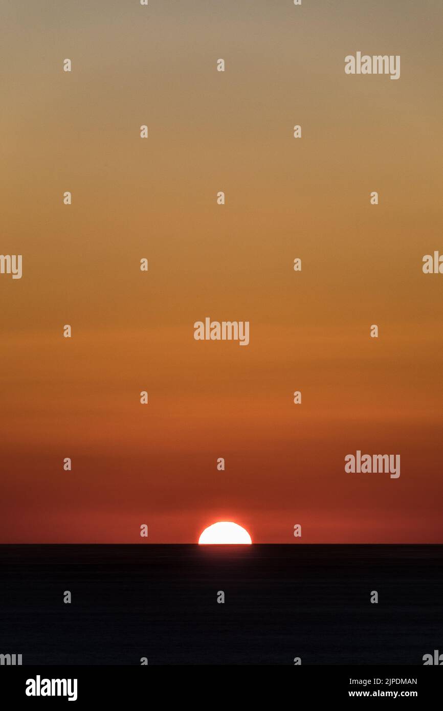 The semi circle of a setting sun as it dips below the sea off the coast ...