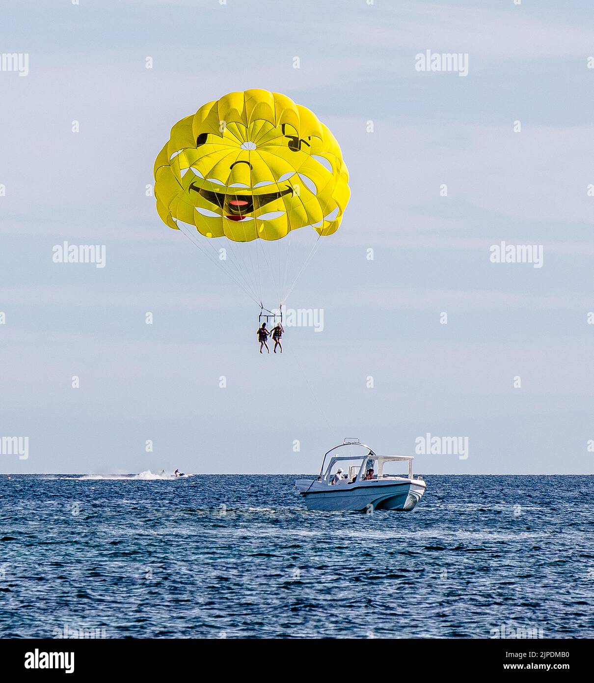 2 people paragliding with a yellow parachute with a smiley face on ...