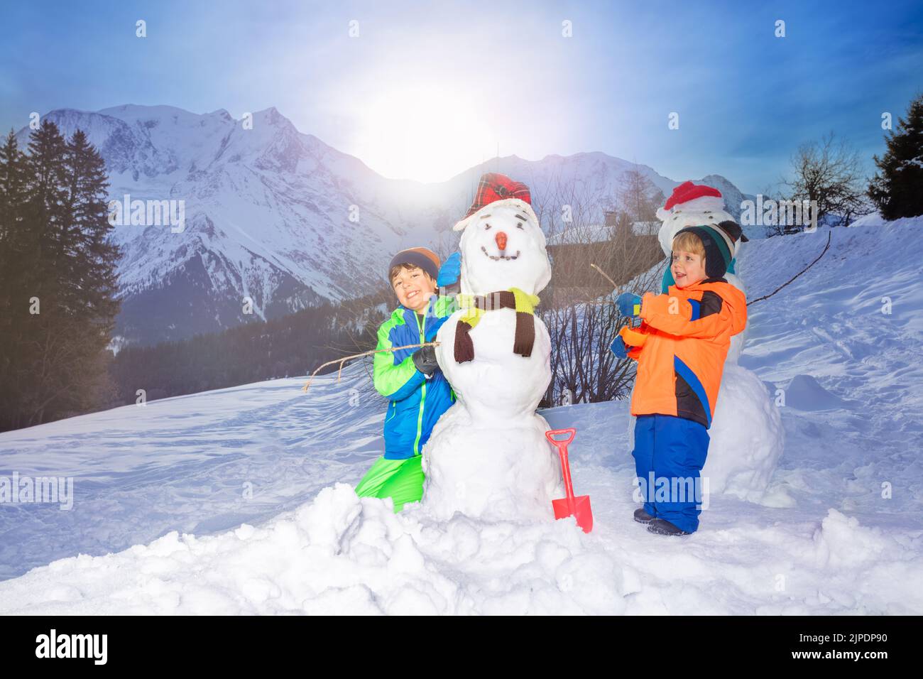 Two boys build, dress snowman at mountains on winter vacation Stock ...