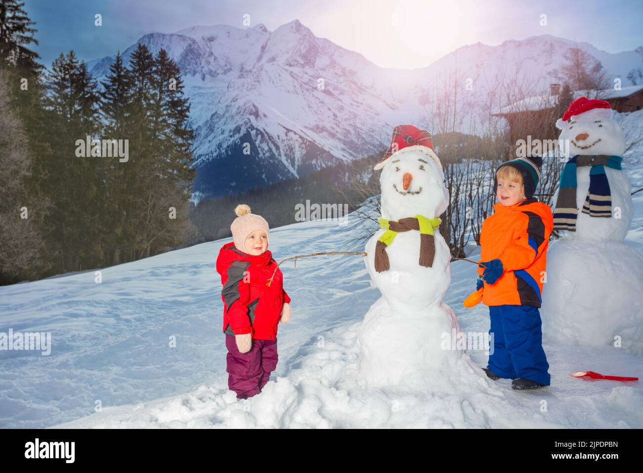 Kids boy with sister girl build, dress snowman at the mountains Stock ...