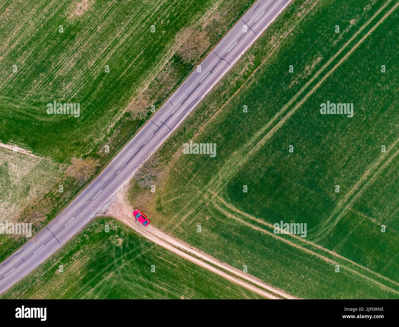 Red car is parking on the green field near the asphalt road. Aerial top ...