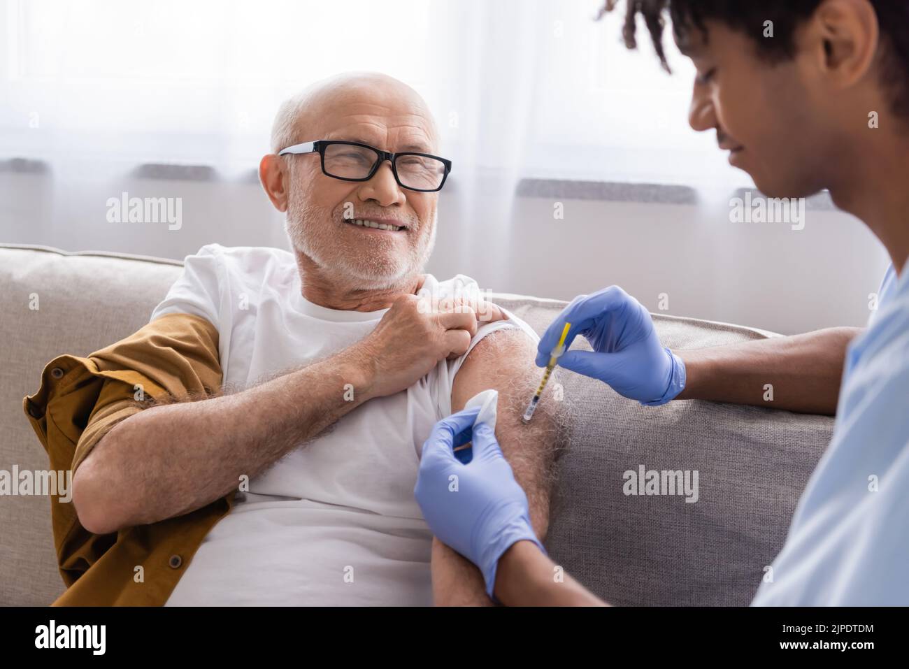 African american nurse doing injection to smiling elderly man at home ...