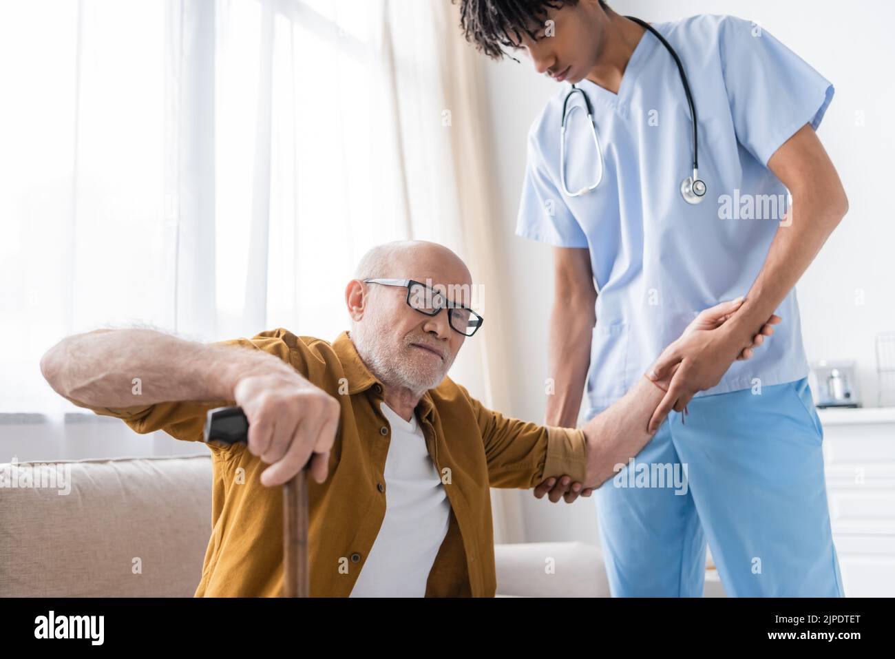 African american nurse helping to elderly patient with walking cane at ...