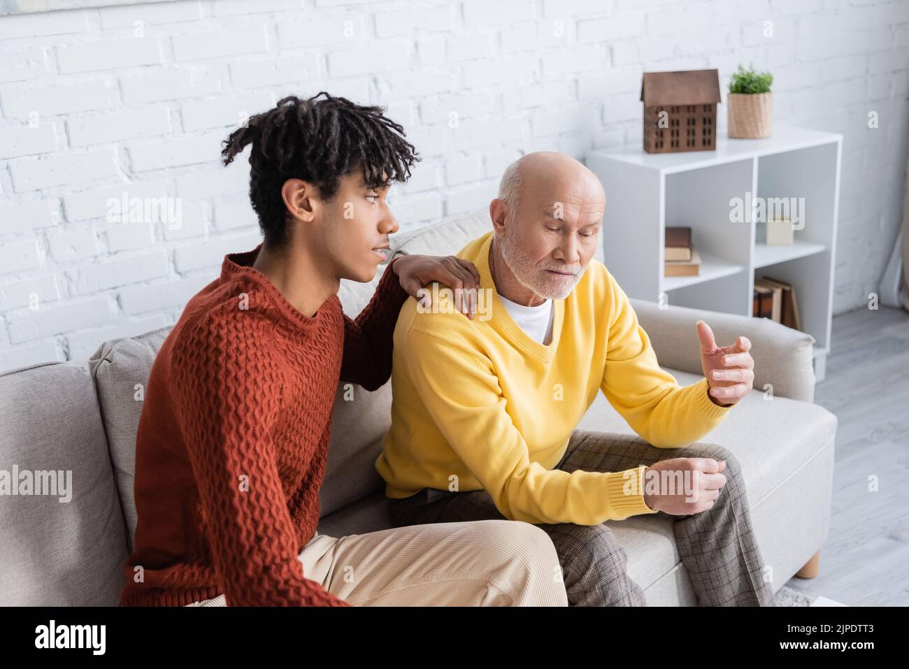 African american grandson touching elderly grandpa in living room Stock ...