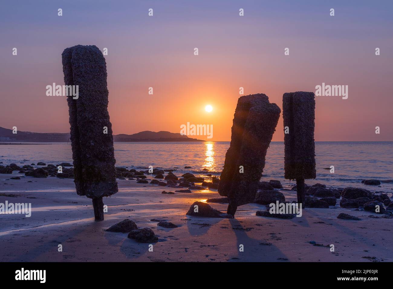 A setting sun with 3 broken parts of a breakwater sticking up out of ...