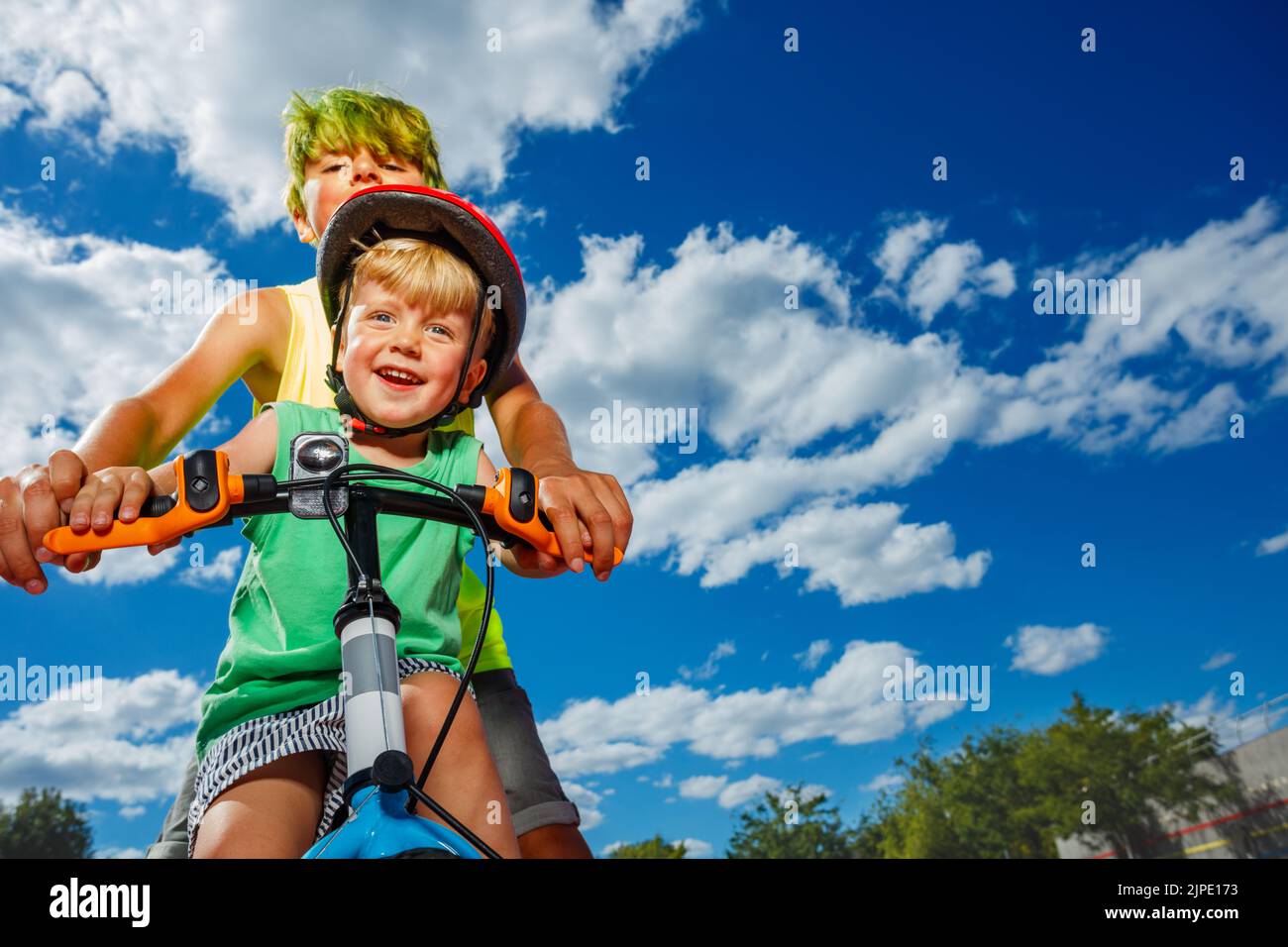 Close-up image big boy push little brother teach to ride a bike Stock Photo - Alamy