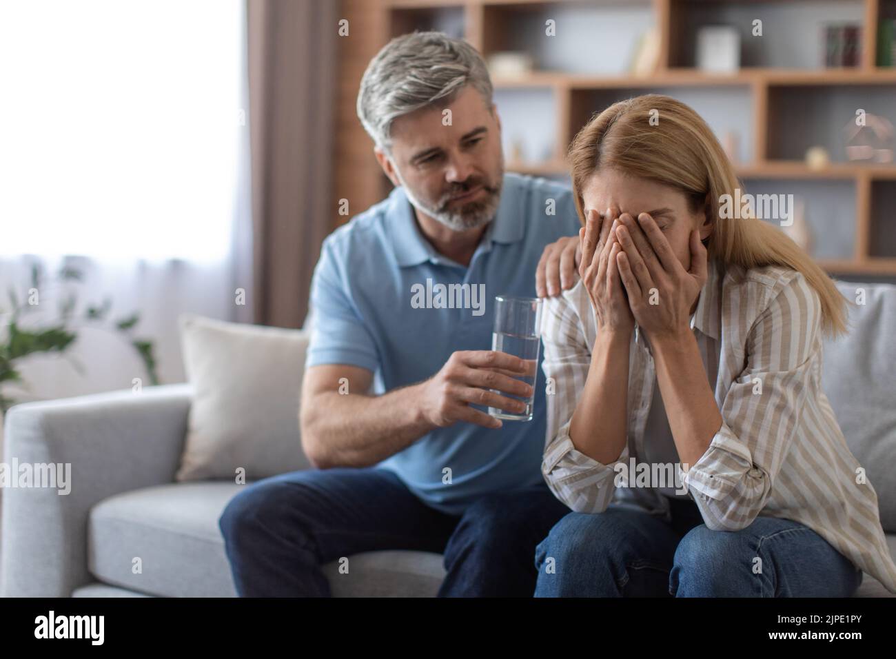 Serious mature caucasian husband calm upset crying wife, gives glass of ...