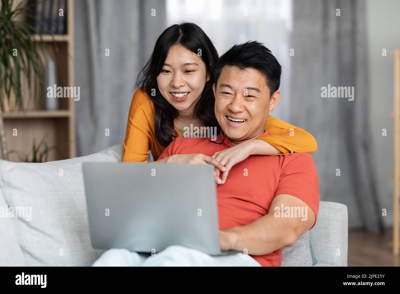 Positive asian couple using computer at home, copy space Stock Photo ...